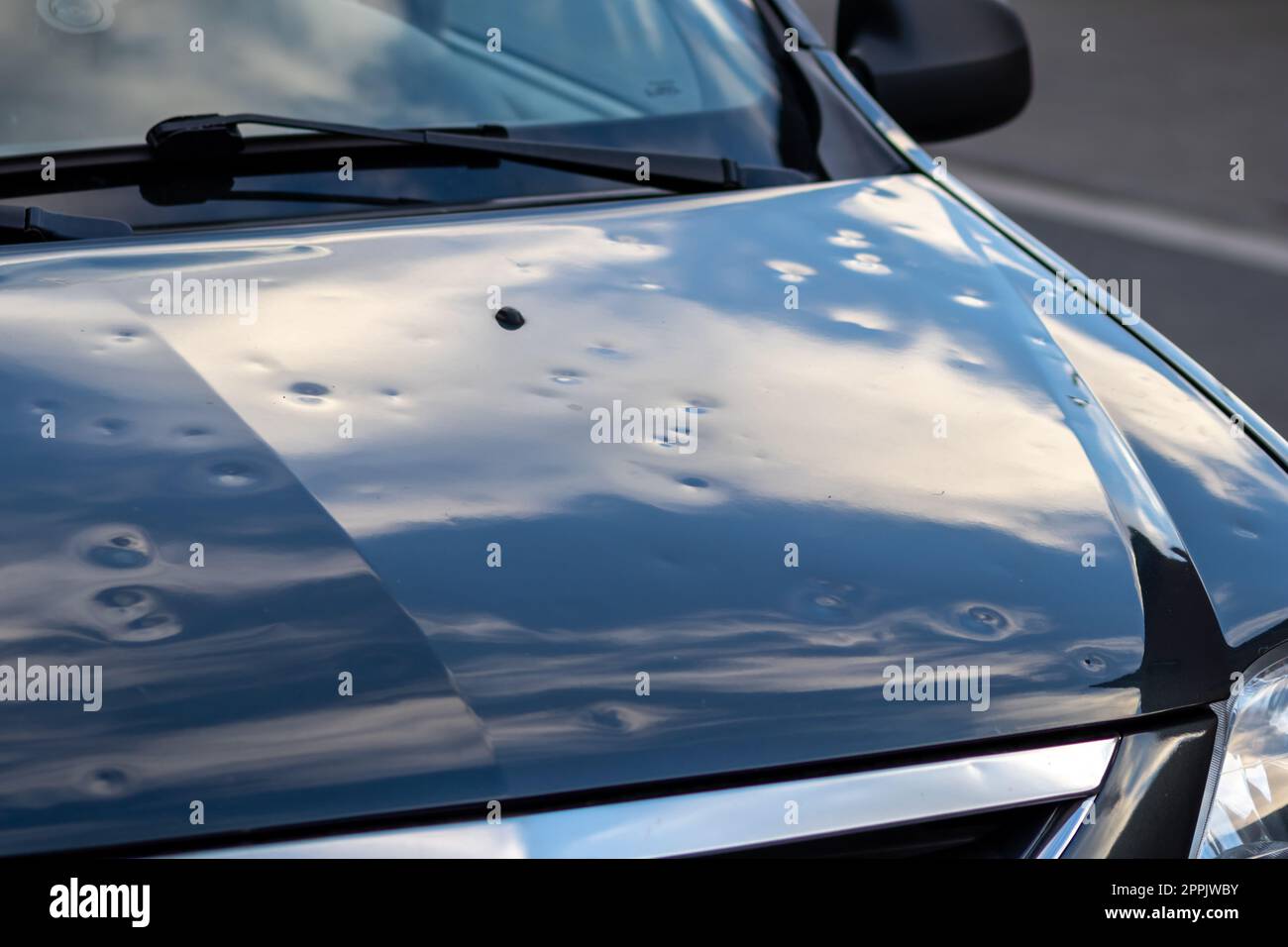 Black car engine hood with many hail damage dents show the forces of ...