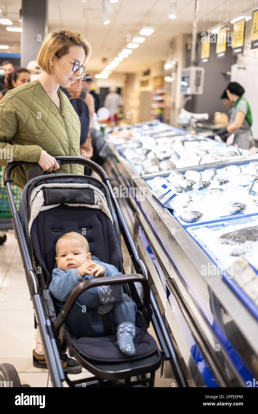 Casualy dressed mother choosing fish in the fish market department of ...
