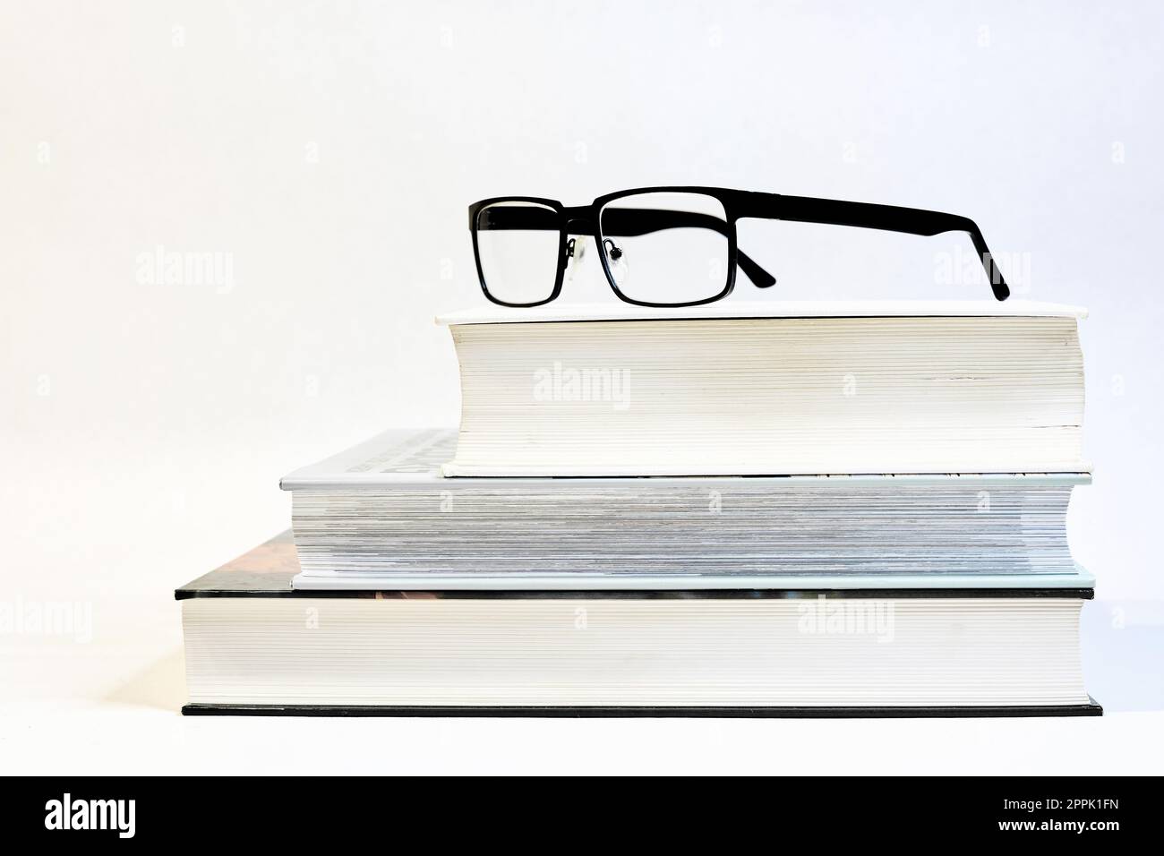 three thick books on a table with glasses as a visual aid and a white ...