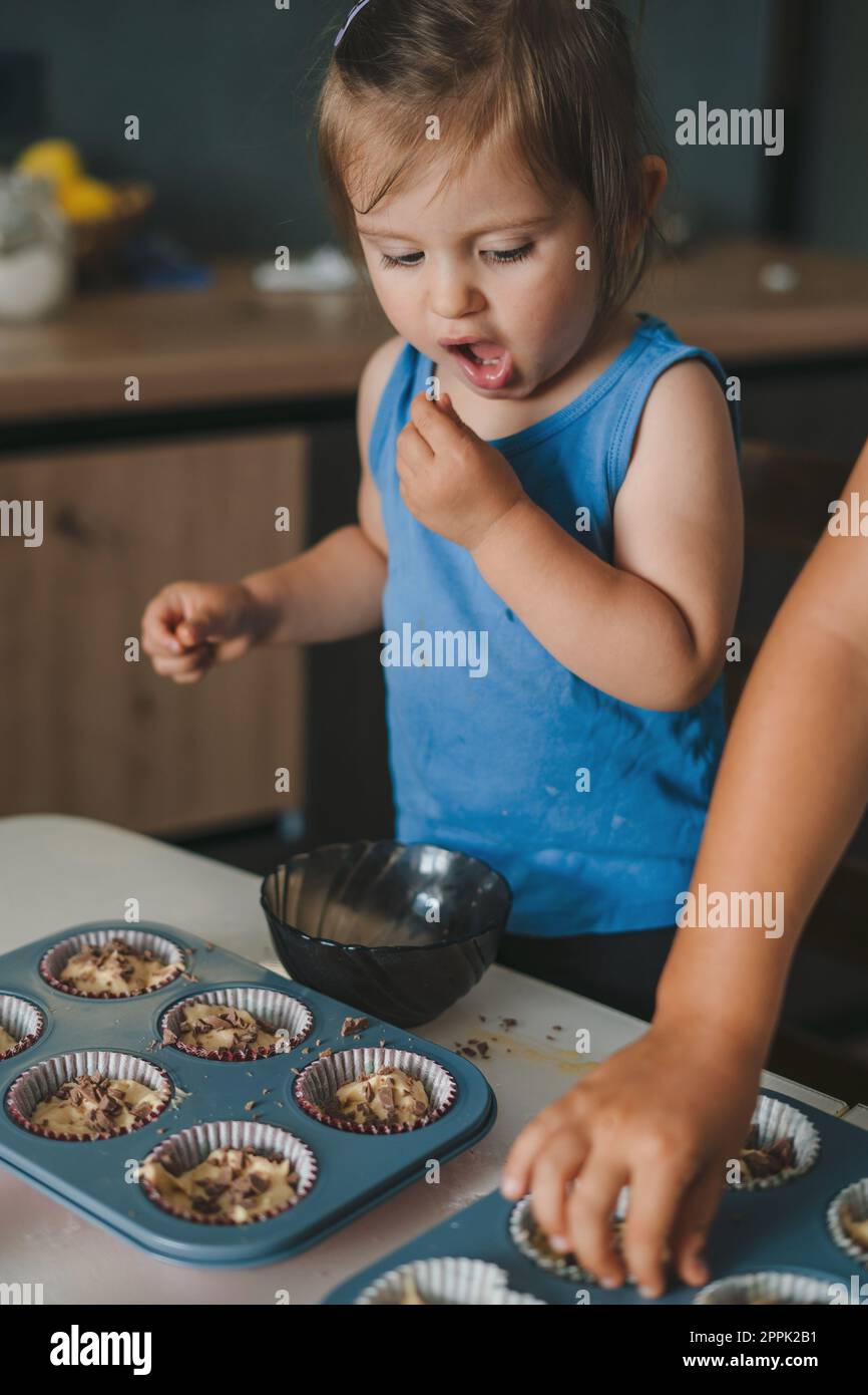 Cute little baby gir spooning muffin batter into the baking cups and ...