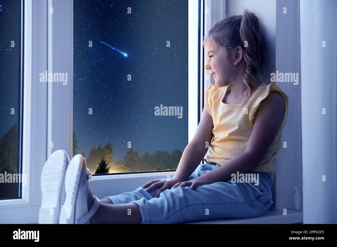 Cute little girl sitting near window and looking at shooting star in ...