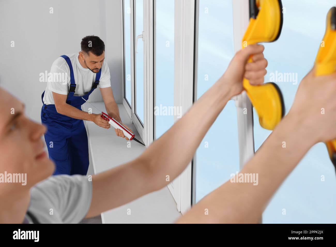 Workers with tube of sealant and suction lifters installing plastic ...