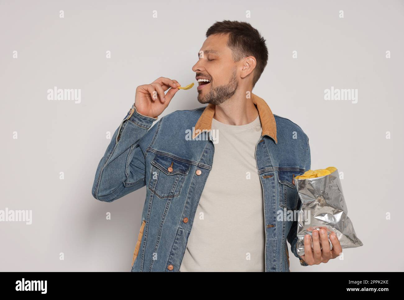 Handsome man eating potato chips on light grey background Stock Photo ...
