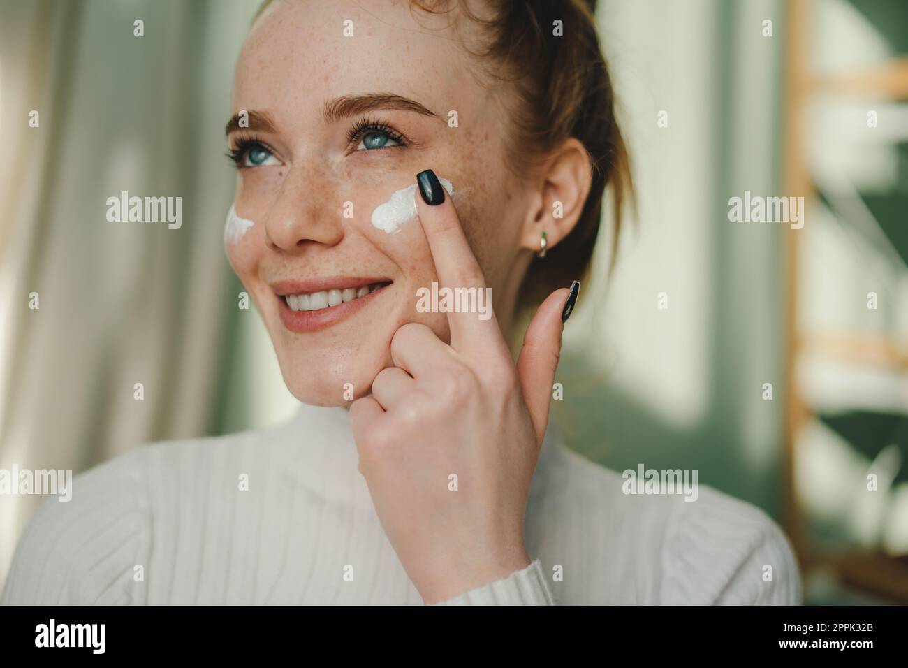 Close-up view of an attractive young adult woman applying facial cream ...