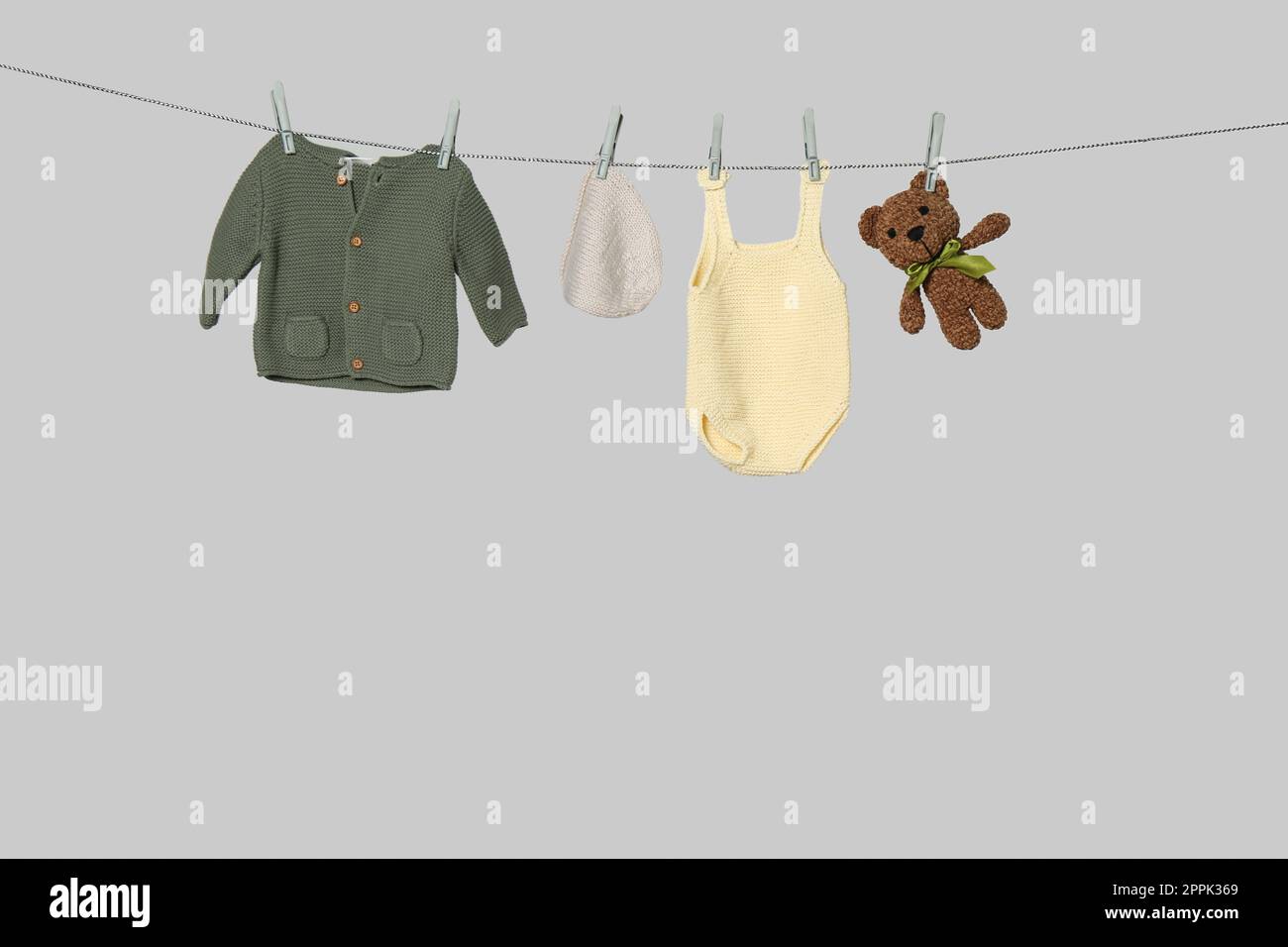 Different baby clothes and toy drying on laundry line against light ...