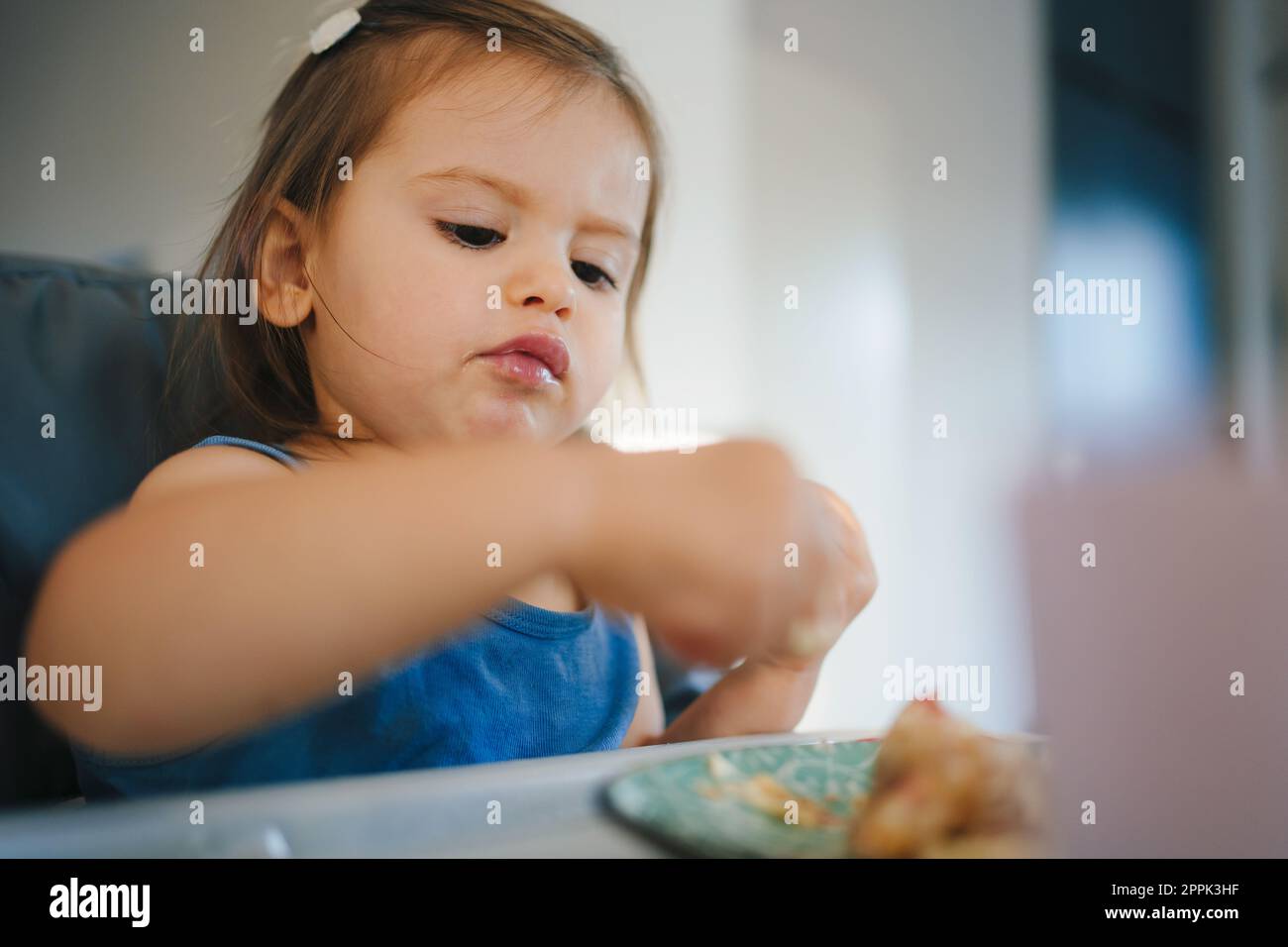 Infant baby girl eating food by herself on baby high chair and making ...