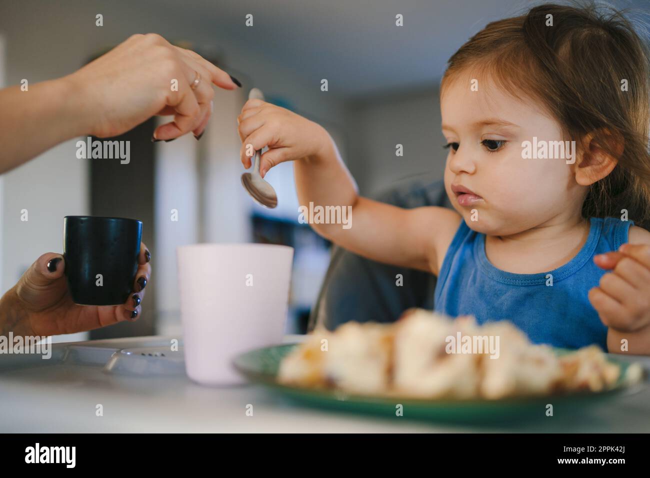 Young baby girl eating learning to eat, feeding herself using spoon ...