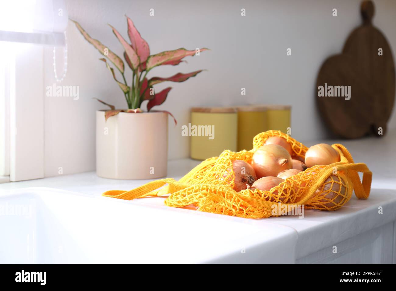 Golden onions in mesh tote bag on countertop of kitchen Stock Photo - Alamy