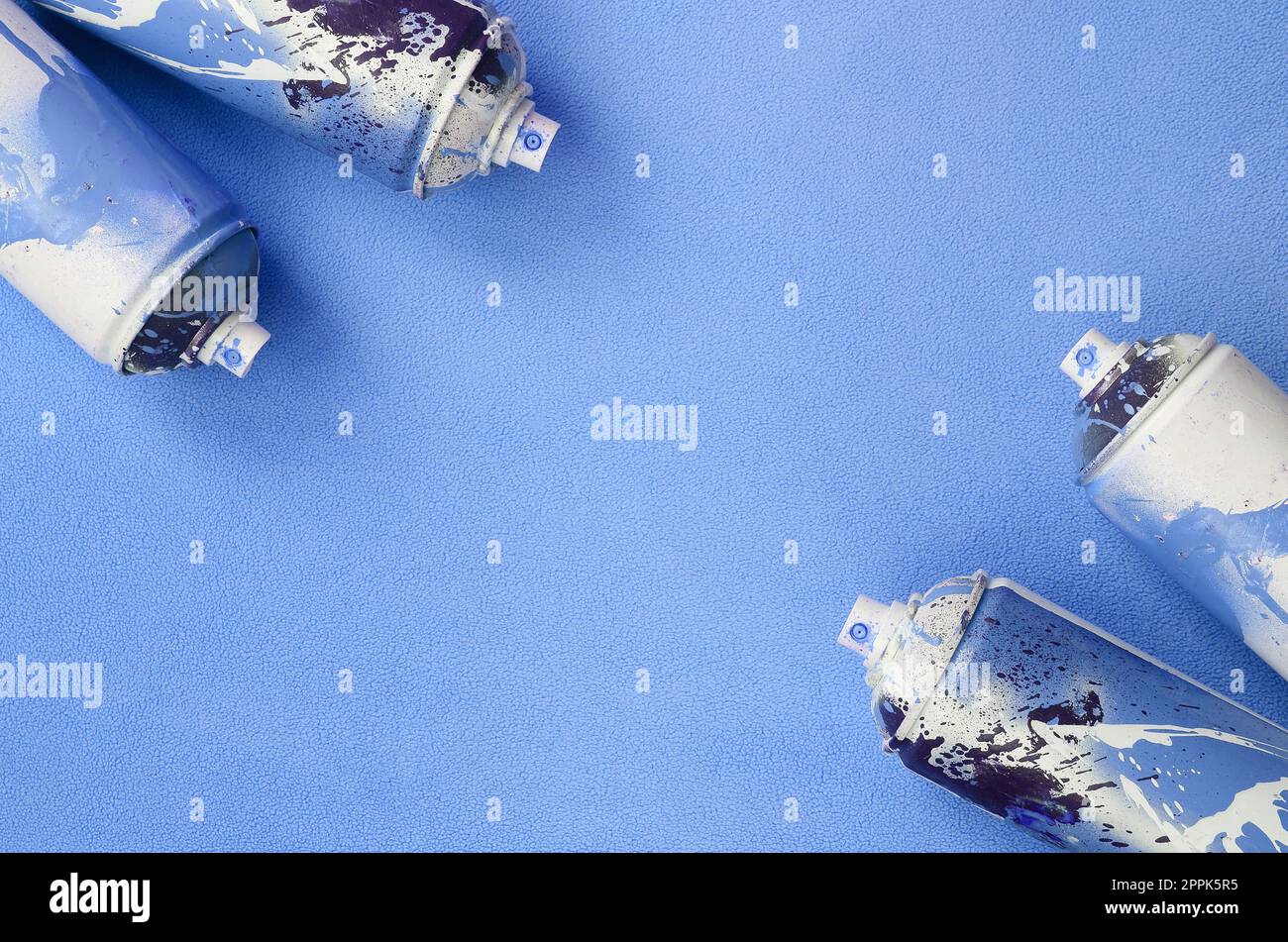 Some used blue aerosol spray cans with paint drips lies on a blanket of ...
