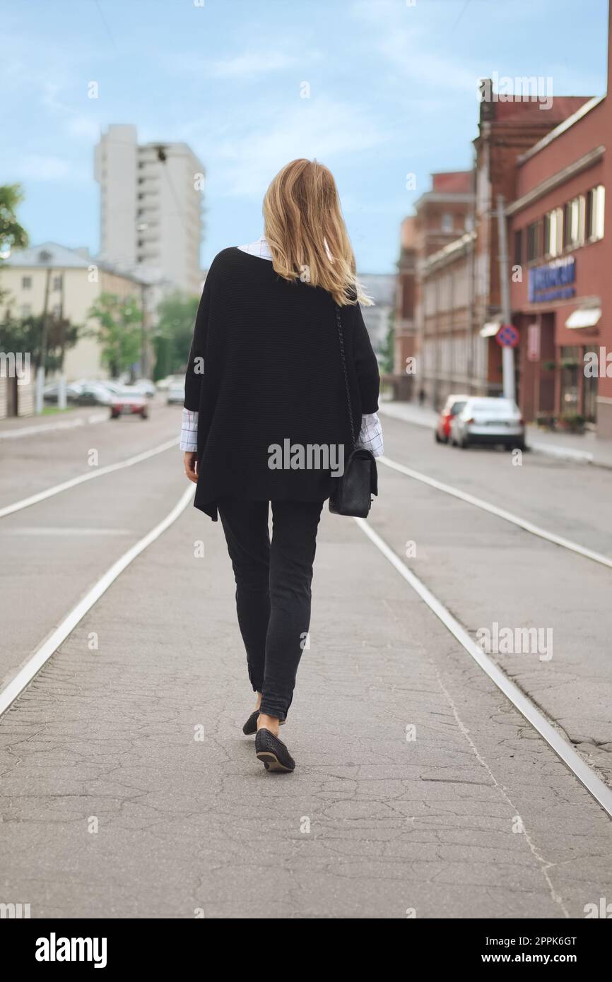 Hipster girl walking on the centre of the street in black poncho and ... Hipster girl walking on the centre of the street in black poncho and ...
