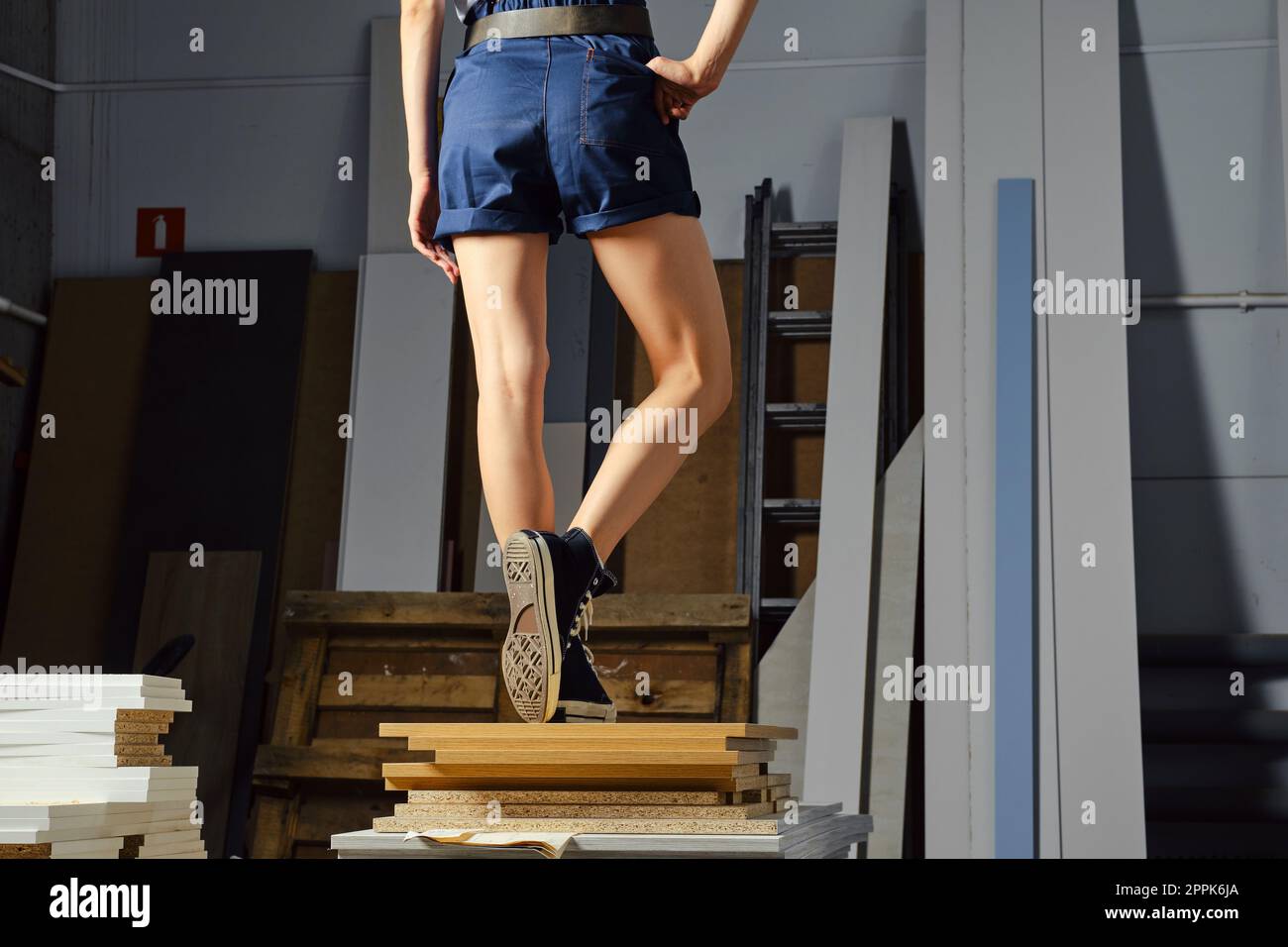 Rear view of a female legs in work clothes on a stack of chipboard ...