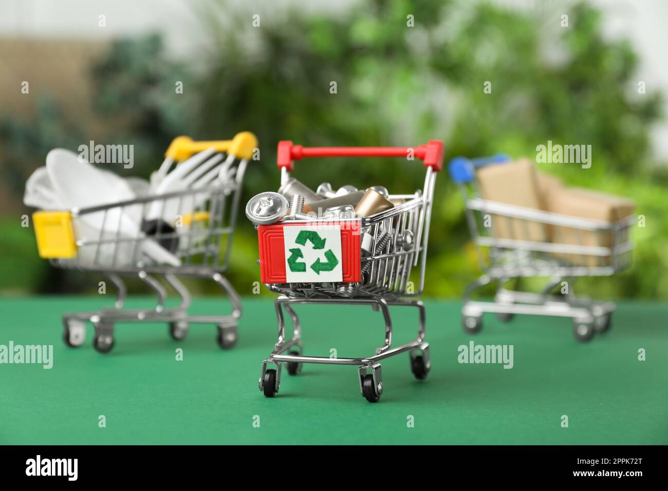 Shopping cart with recycling symbol full of garbage on green table ...