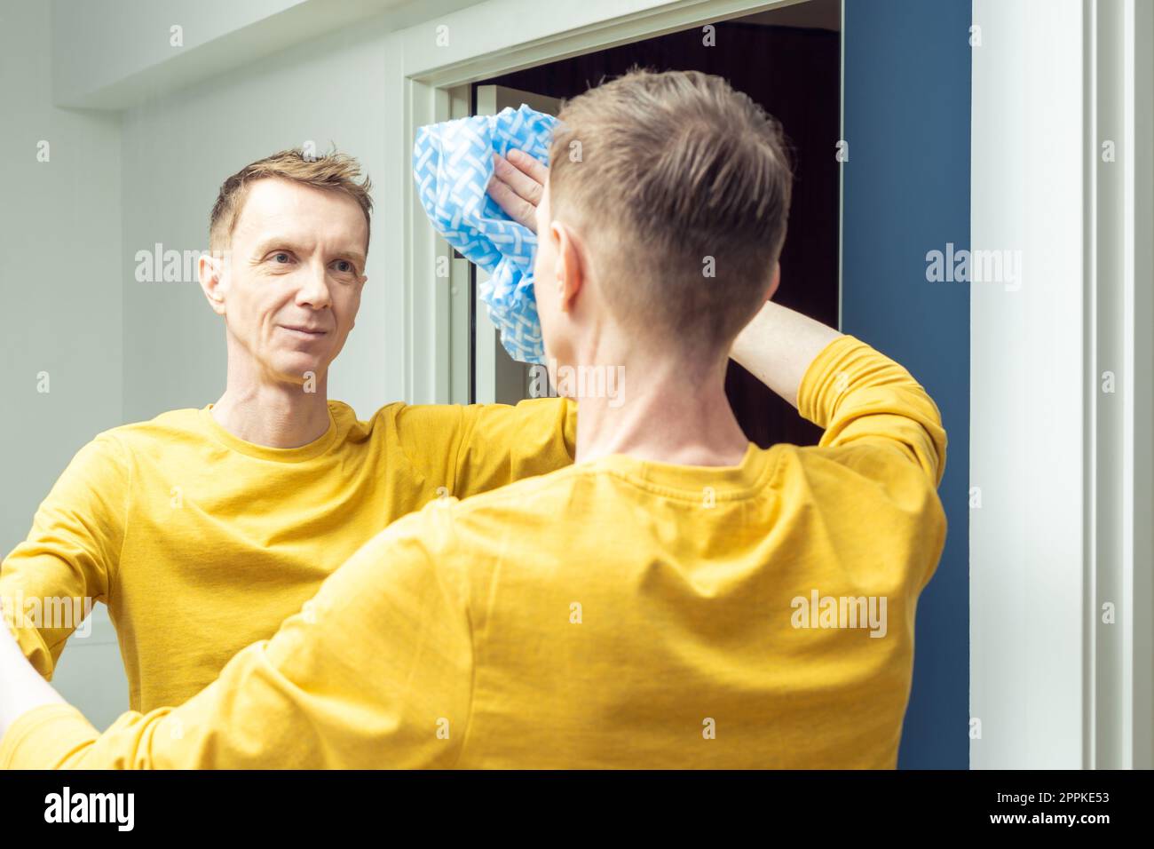 Smiling mature man wiping room mirror with dry rag, back view. Rub from ...