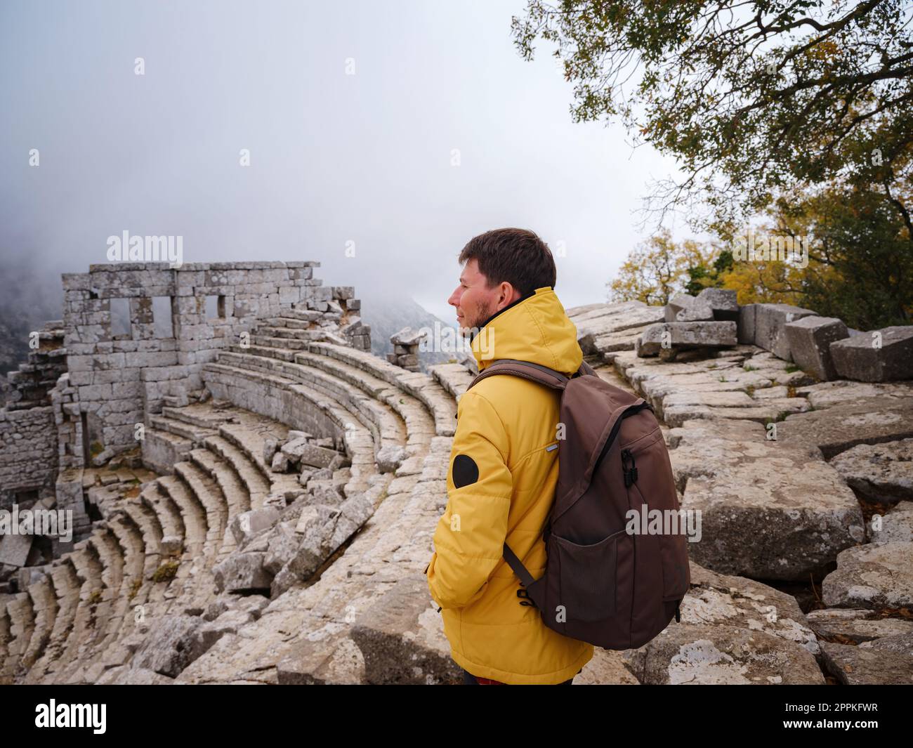 Autumn walk , man in yellow jacket looks at the ancient amphitheatre in ...