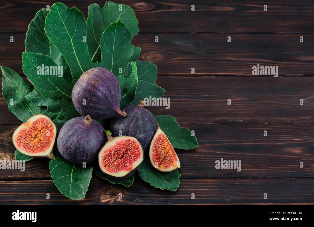 Figs and halves of several fruits on fig tree leaves on an old wooden ...