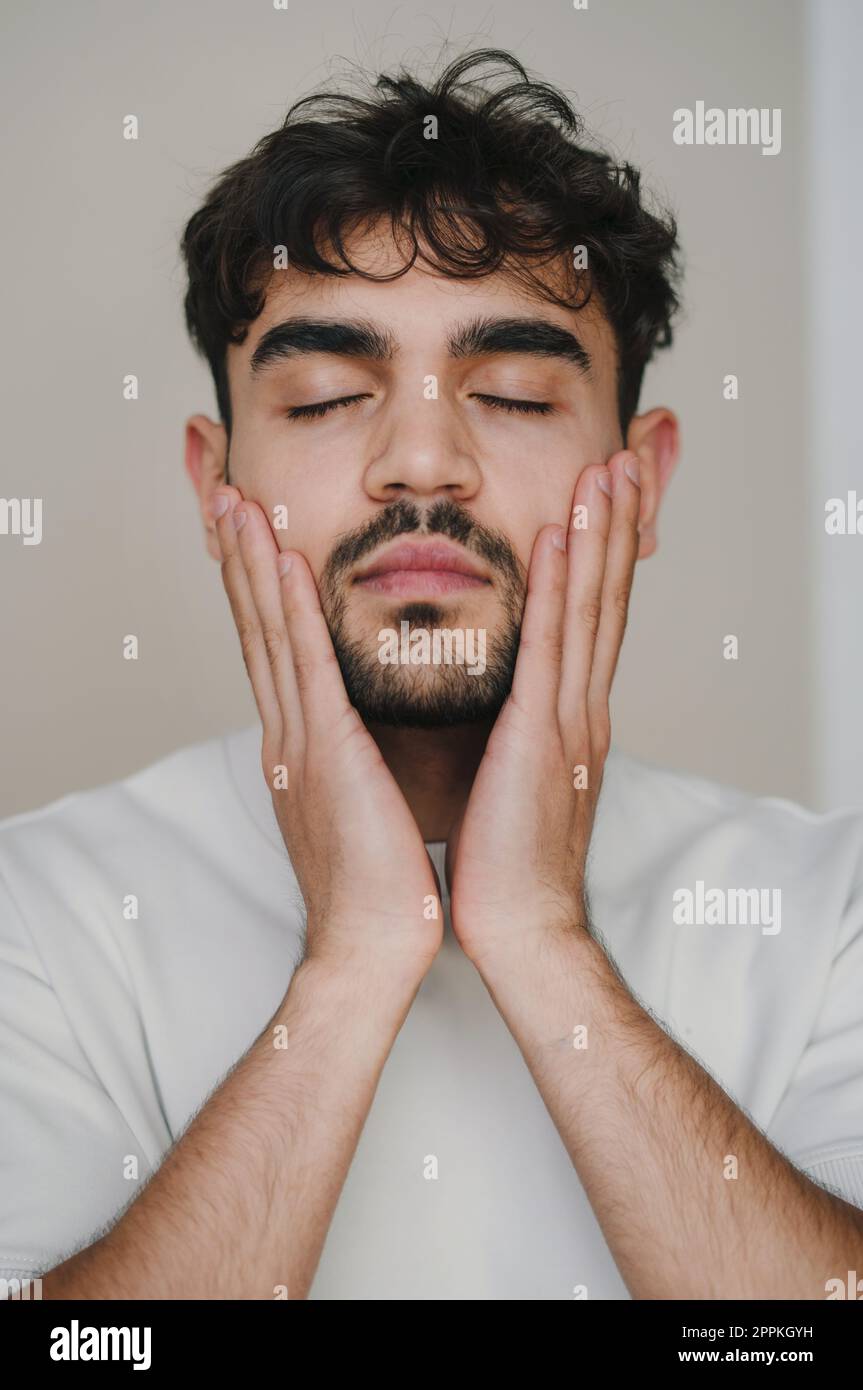 Front view of a young man with eyes closed touching cheeks with hands ...