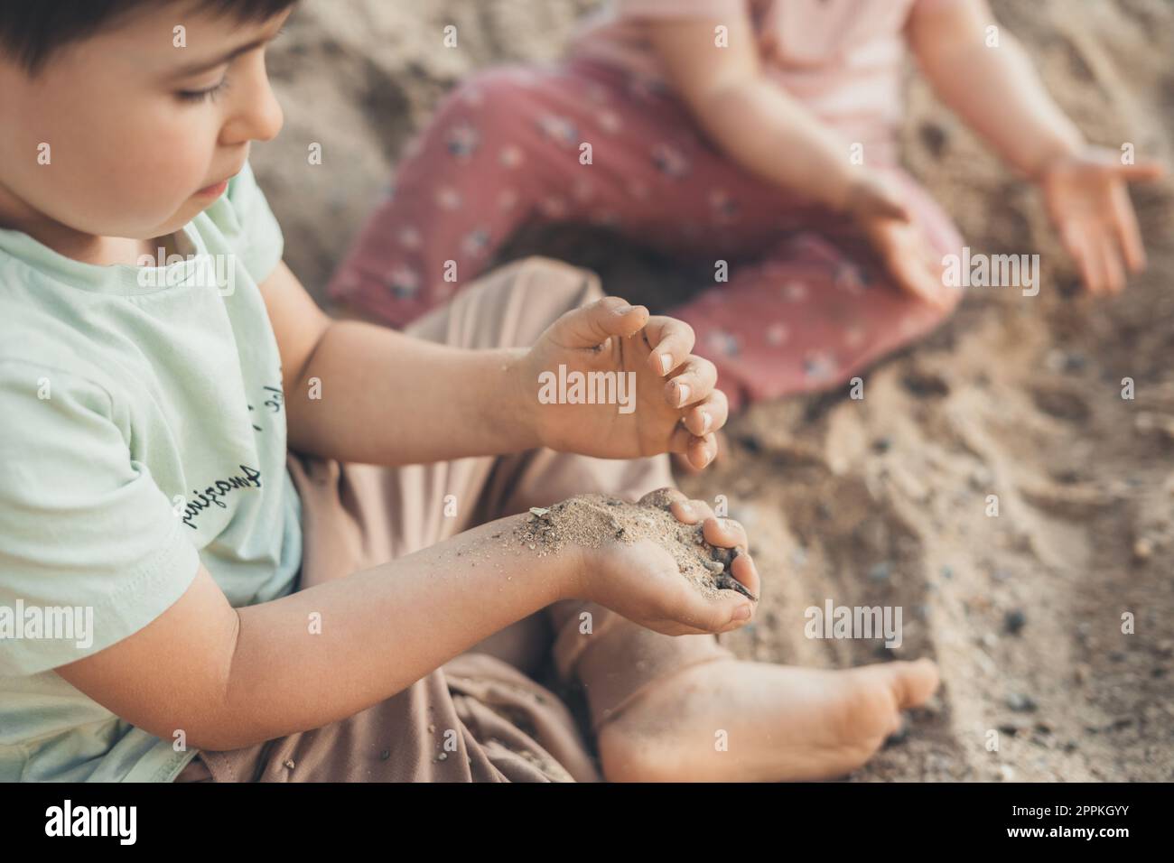 Cute young boy playing in the sand with his little sister, getting ...