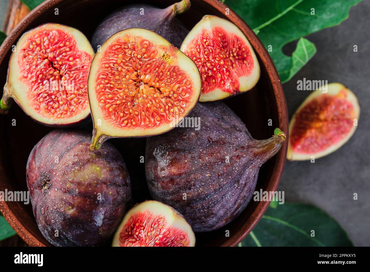Fresh figs and fig halves on a brown old clay plate. Dark background ...
