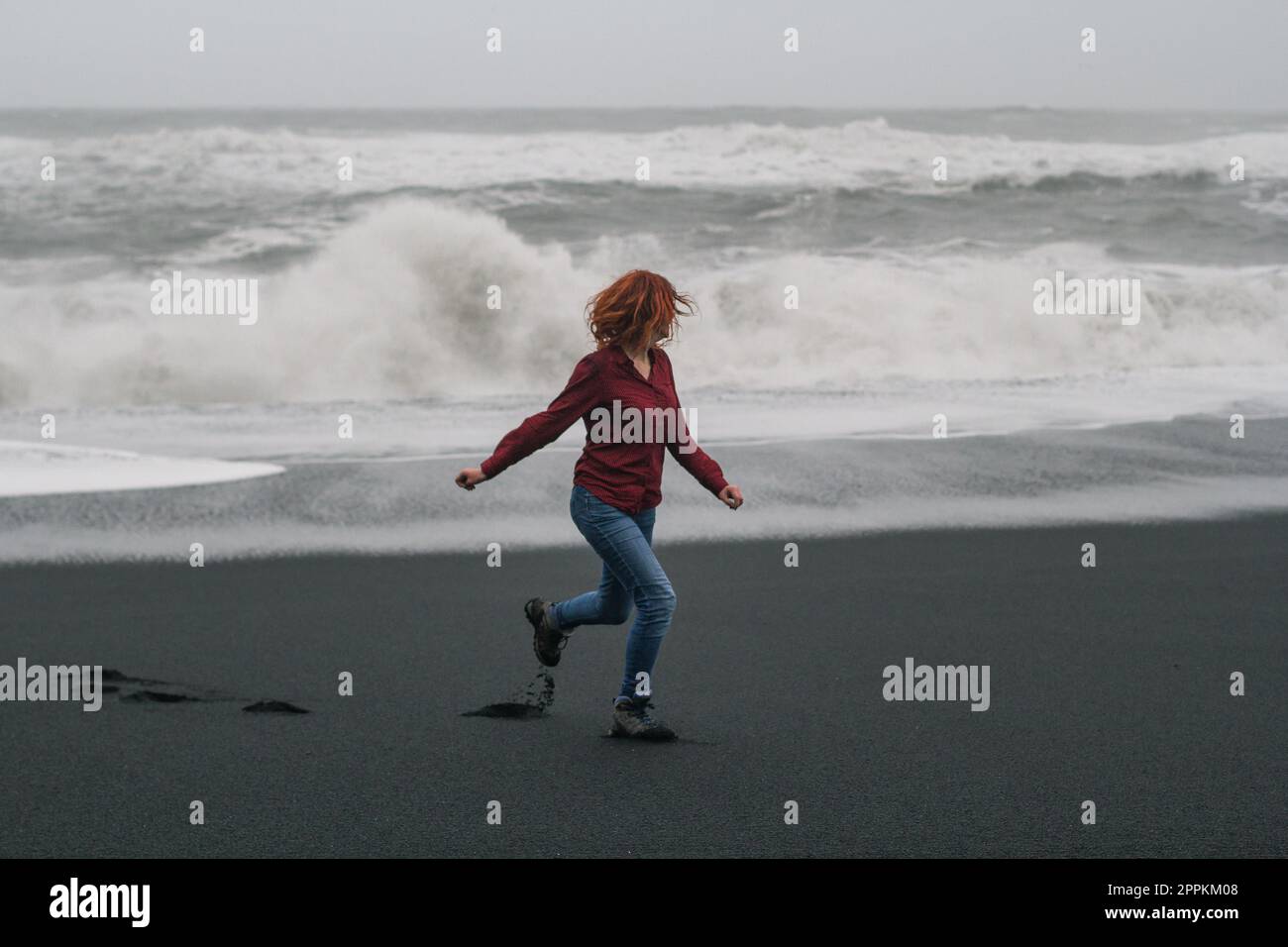 Redhead lady running along black beach scenic photography Stock Photo ...