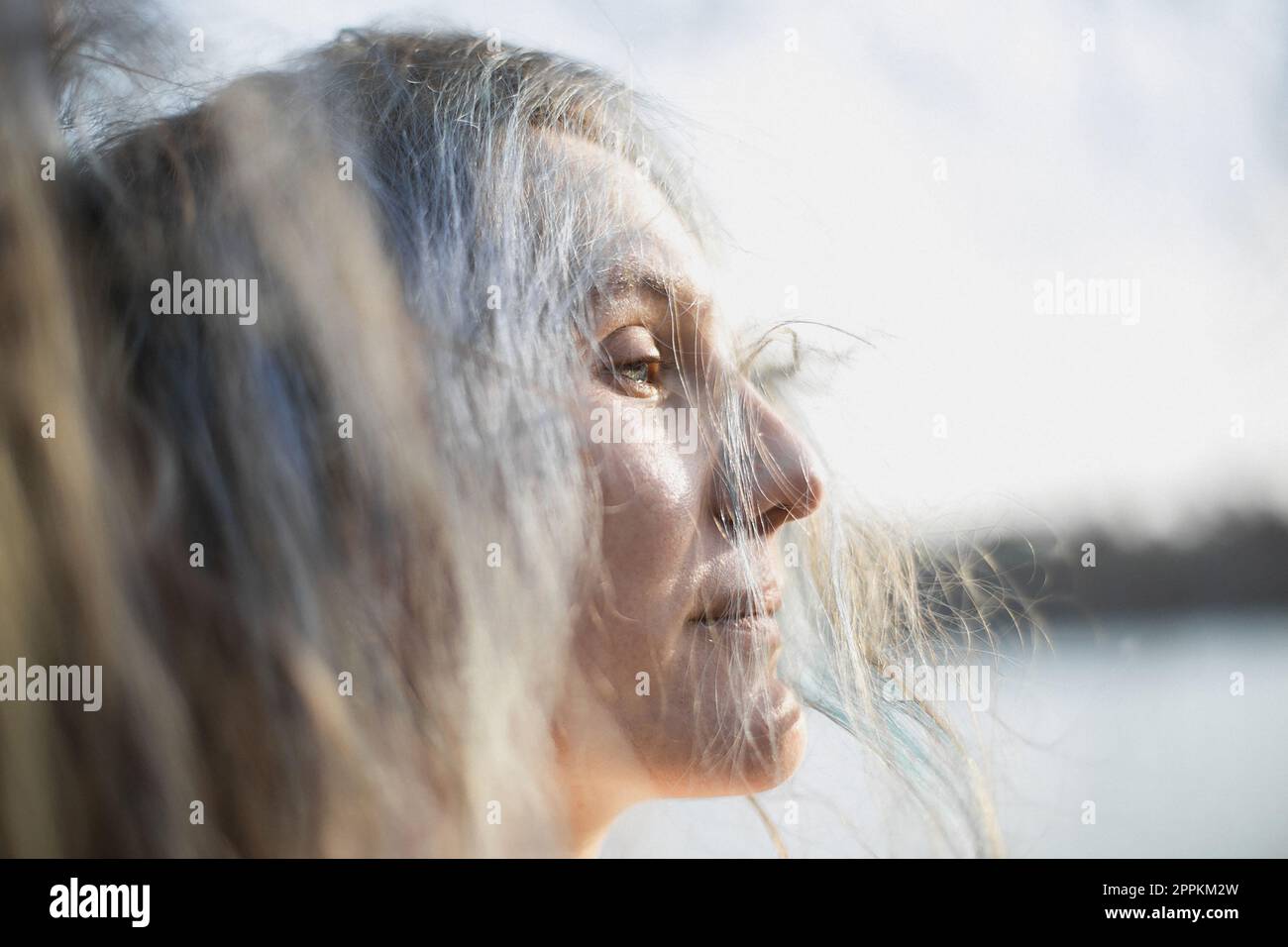 Close up woman with half closed eyes and silver hair falling on face ...