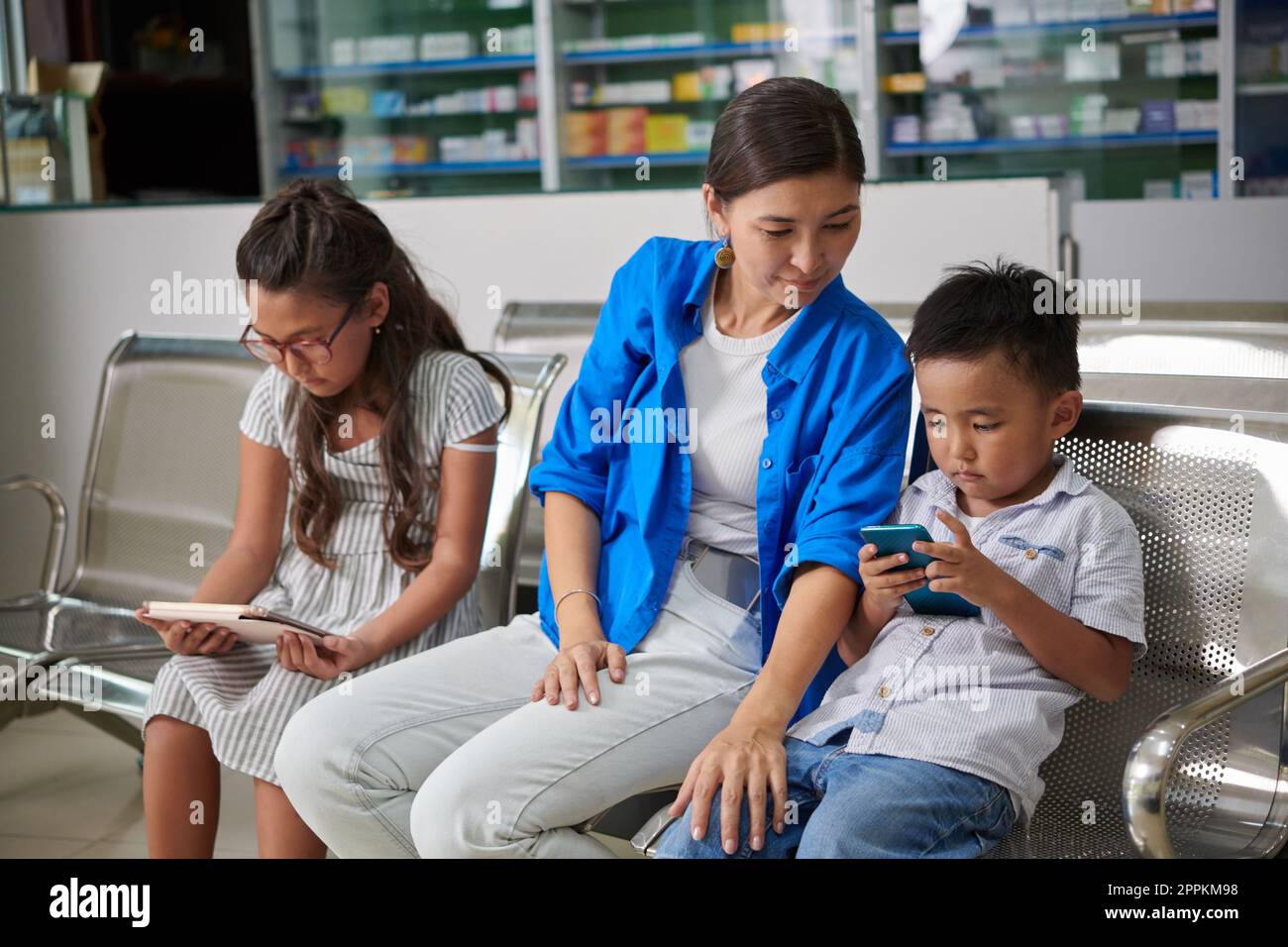 Mother and two kids waiting in hall of hospital, watching videos on ...