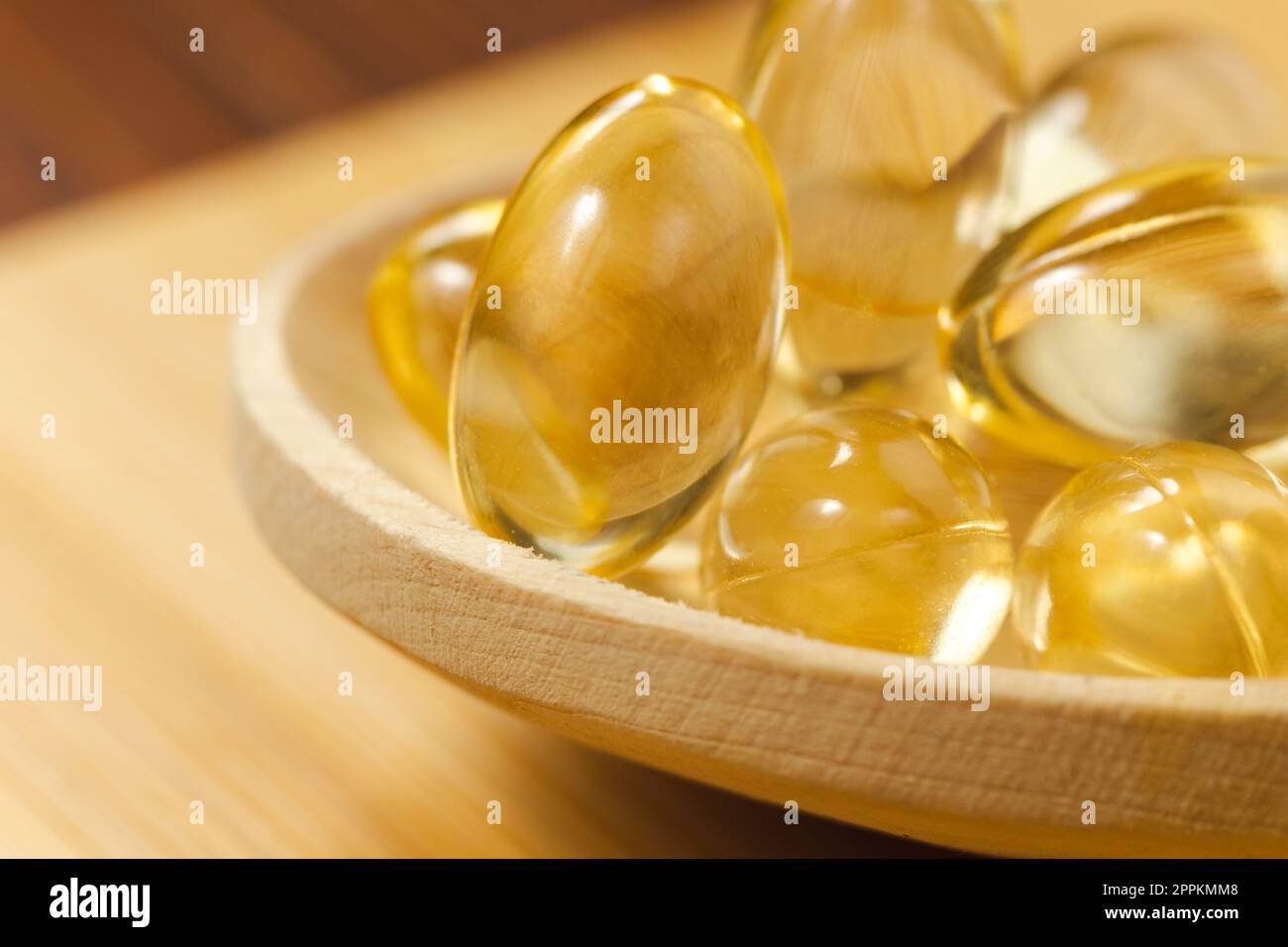 Yellow oil soft gel capsules in wooden background. Cosmetic pill capsule of vitamin E, A, almond ...