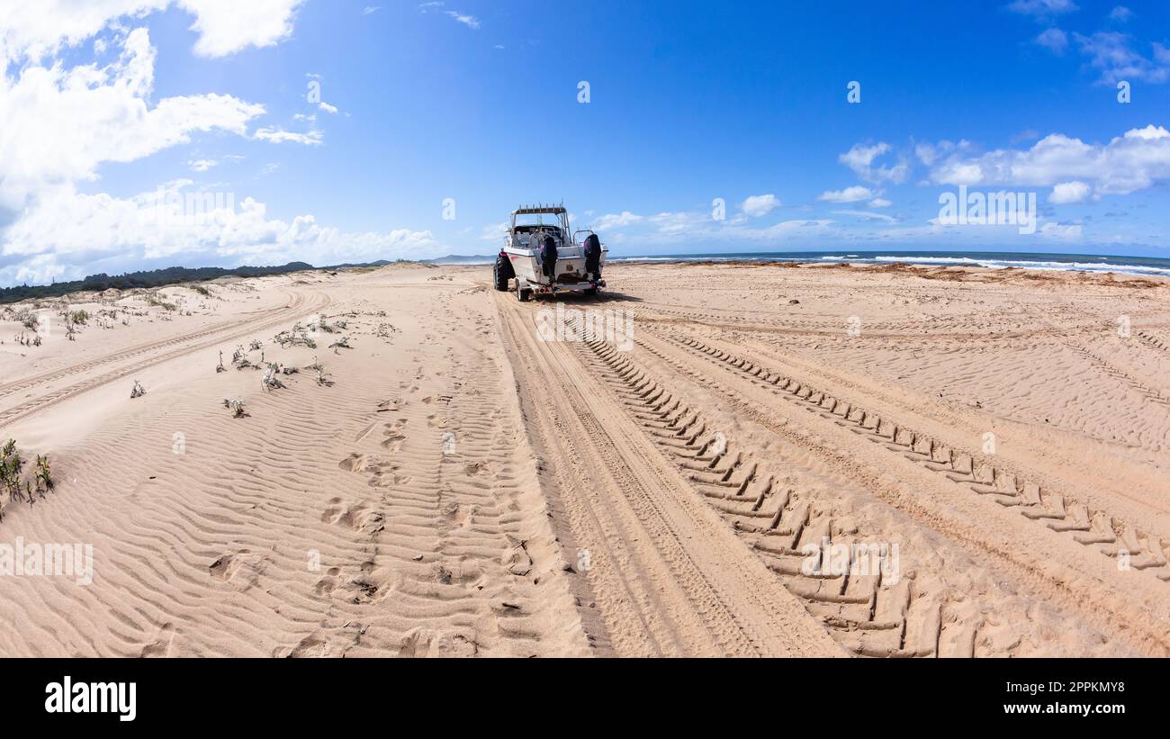 Tractor towing fishing boat trailer on beach sand along waters edge ...