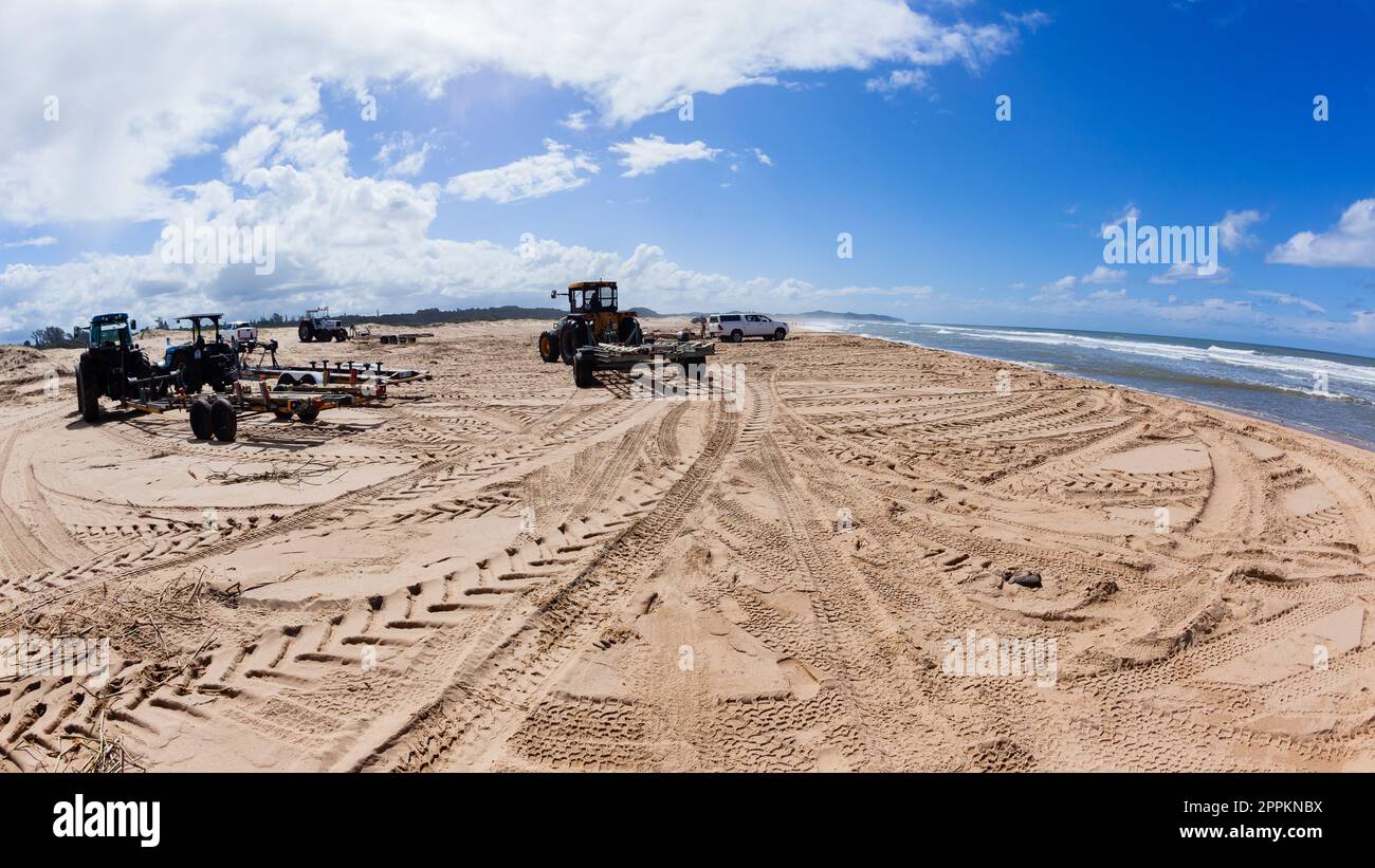 Tractors boat trailers on beach sand along waters edge with boat owners ...