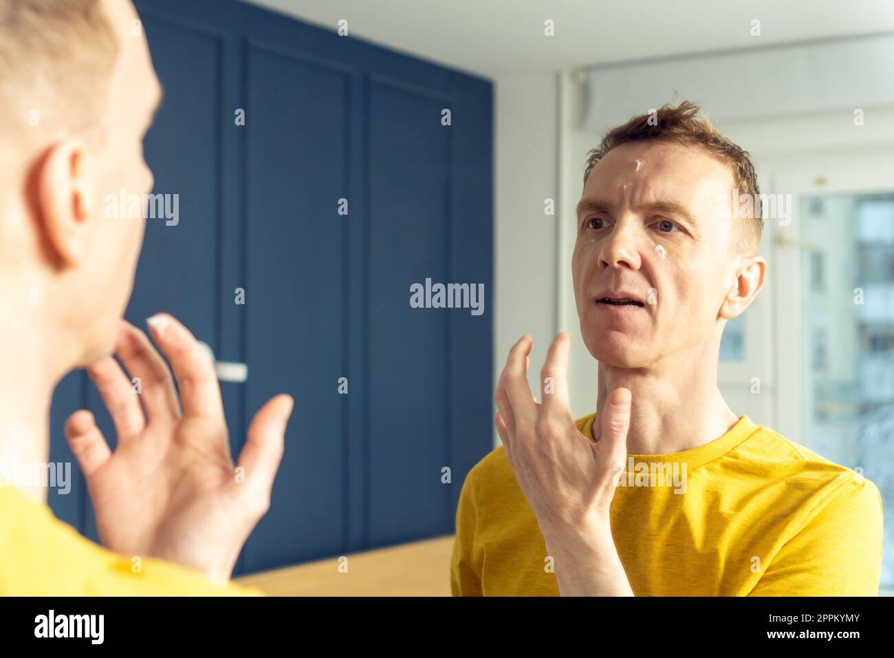Middle aged man apply moisturizing cream with finger on clear facial areas. Male portrait in ...