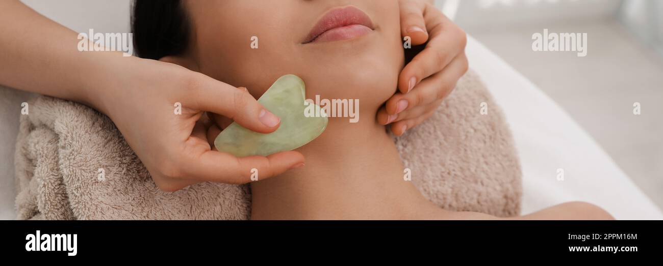 Young woman receiving facial massage with gua sha tool in beauty salon. Banner design Stock ...