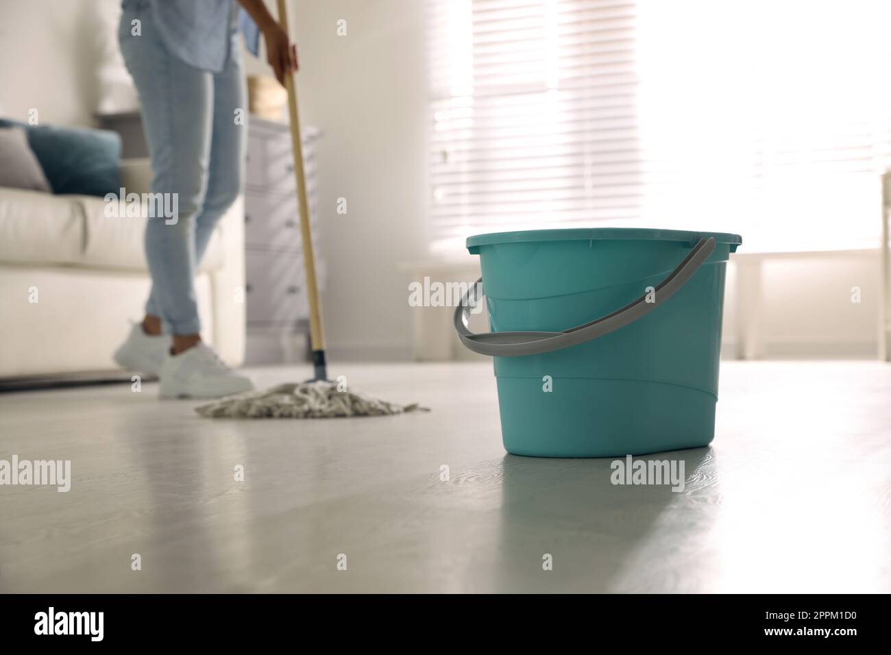 Plastic bucket and woman mopping floor in living room, closeup ...