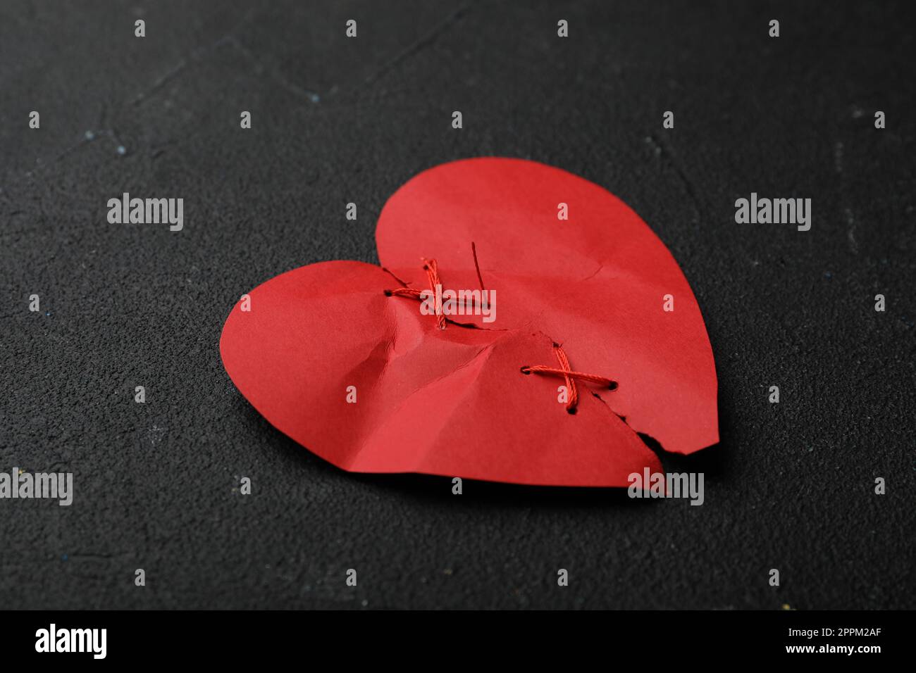 Torn paper heart sewed with thread on black stone background ...
