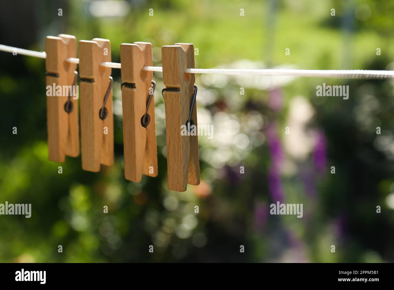Wooden clothespins hanging on washing line outdoors, closeup. Space for ...