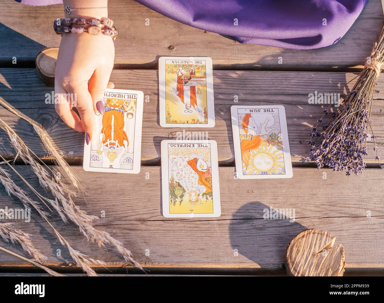 Woman's hand with purple nails lays one of four Tarot cards spread out ...