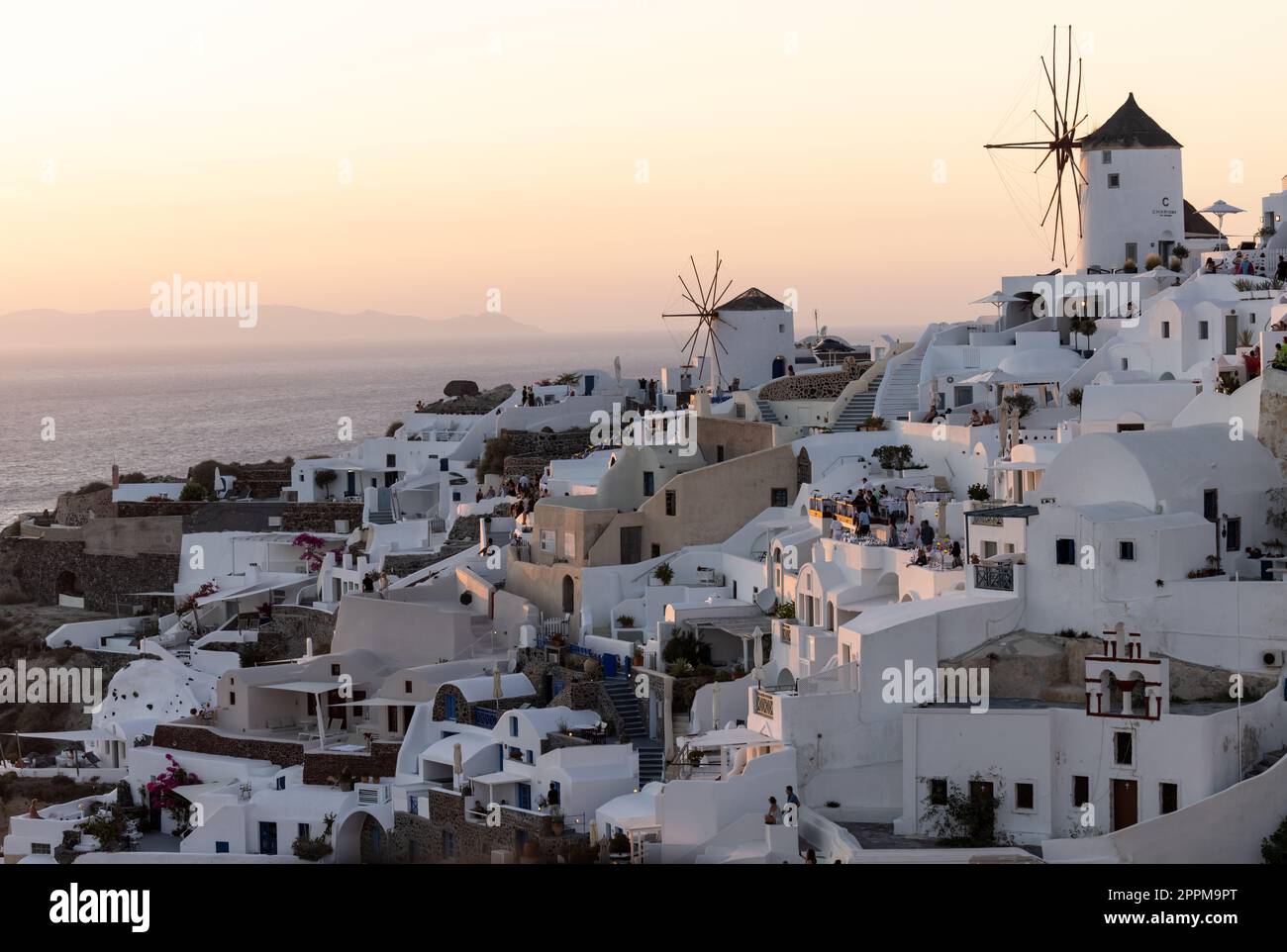 Whitewashed houses and windmills in Oia in warm rays of sunset on ...