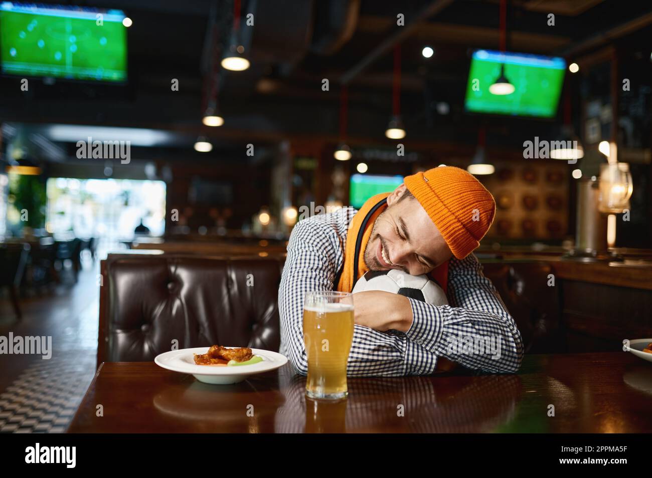 Funny young man soccer fan sleeping on ball while rest in sport bar ...