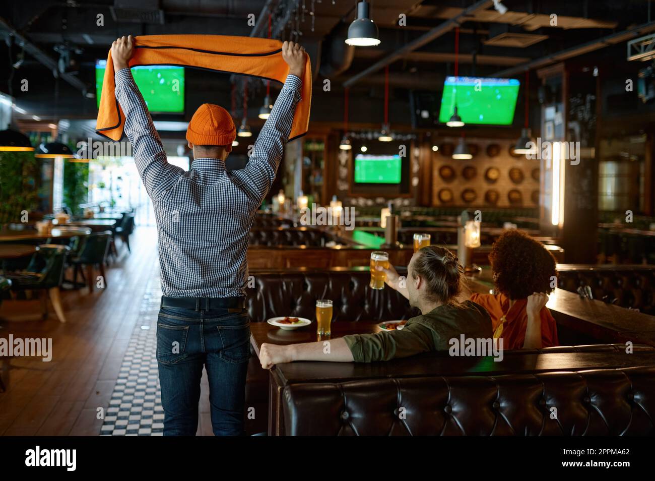 Young excited overjoyed friends watching football match in sports bar ...