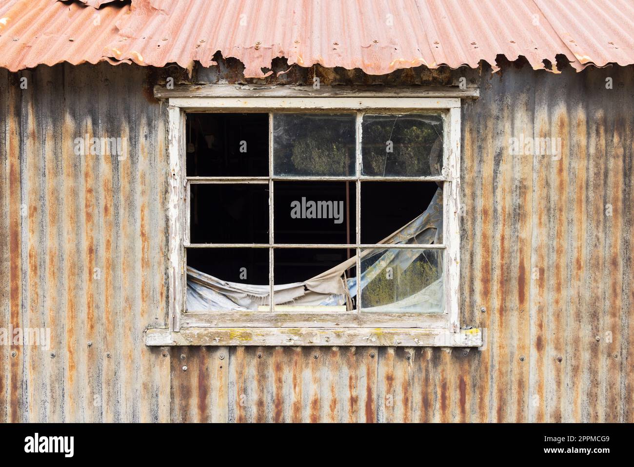 Run down broken window frame within a rusty corrugated metal wall and ...