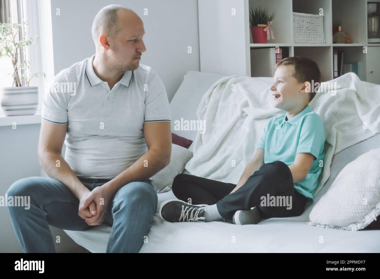 Dad and son sit on couch, talking to each other and smiling Stock Photo ...