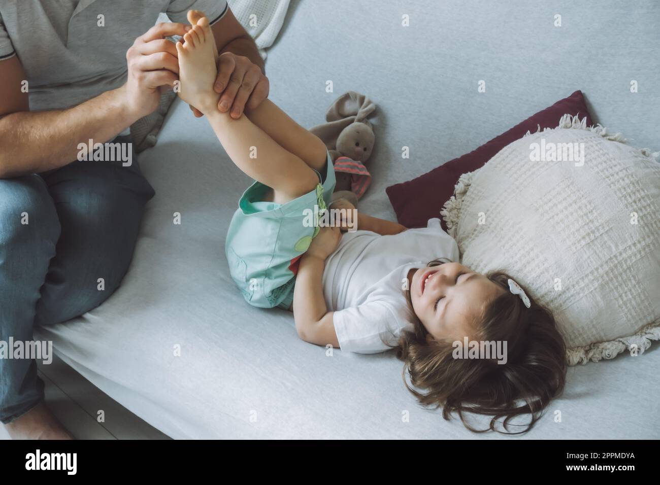 Father plays with little daughter 2-4 on couch. Dad tickles kids feet. Family, having fun Stock ...