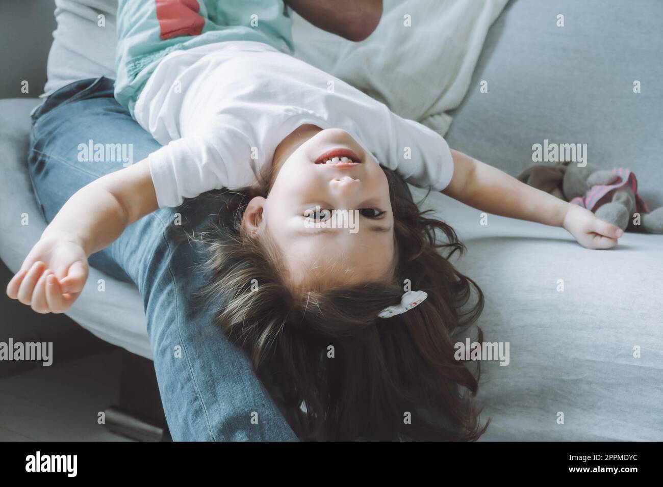Dad and little girl 2-4 play on the couch. Kid lies on father's lap ...