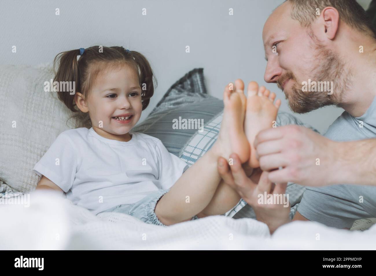 Father plays with little daughter 2-4 on bed. Dad tickles kids feet. Family, having fun Stock ...