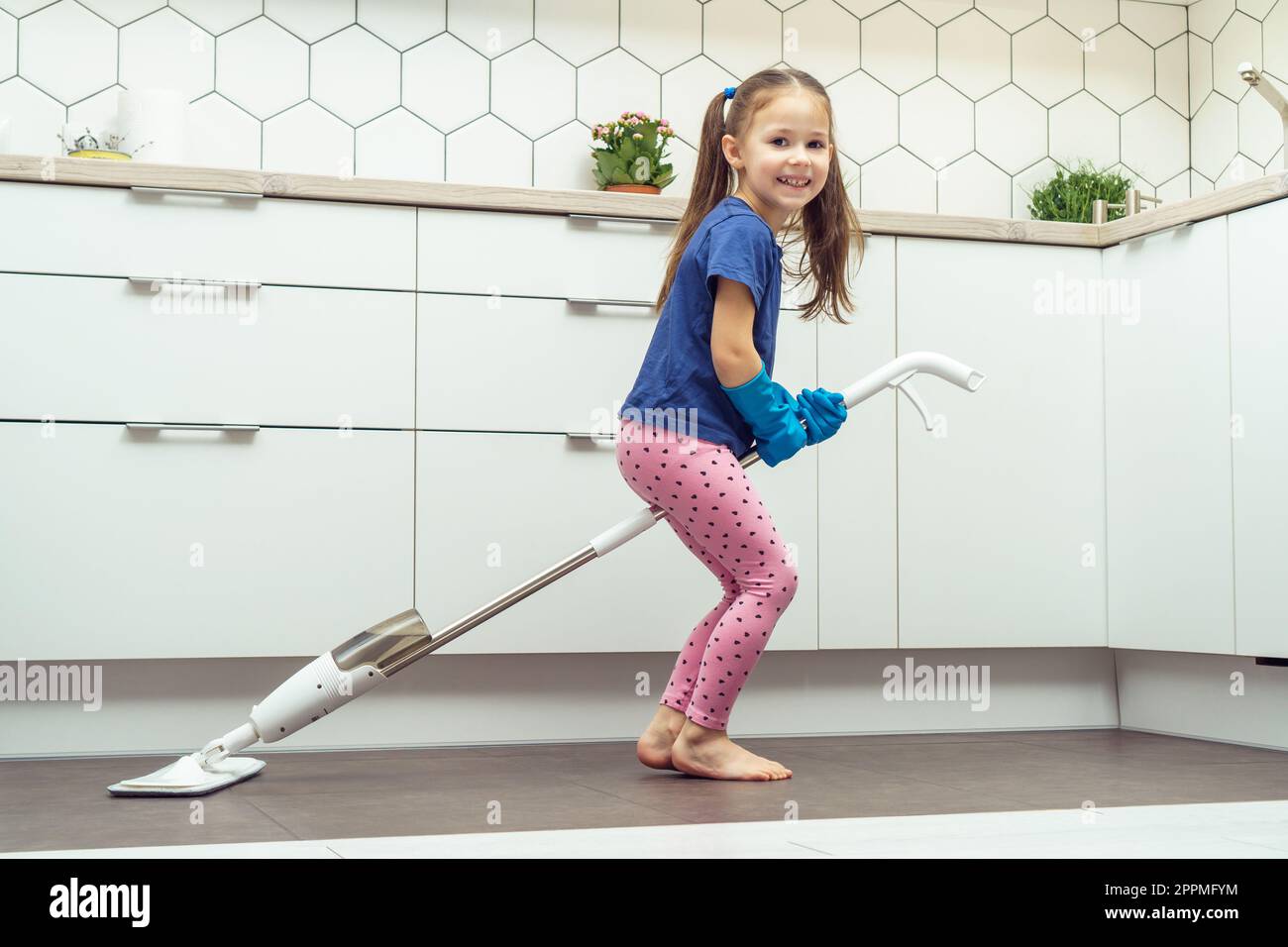 Happy little girl sitting on modern mop for floor washing with ...