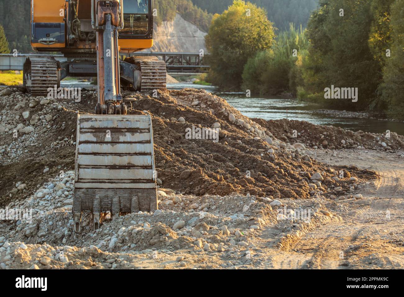 Small yellow excavator at pile of rocks and stones next to river ...