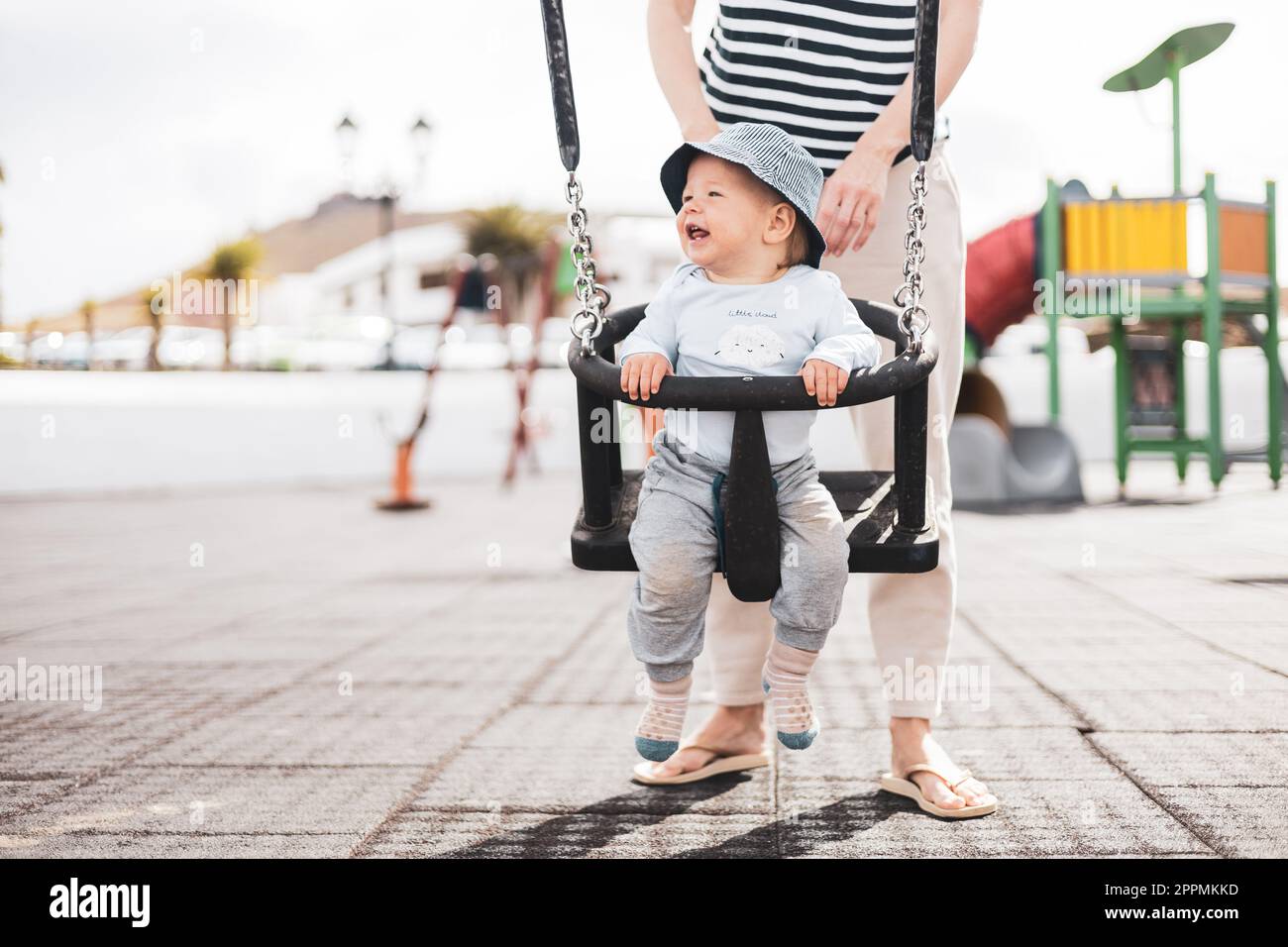 Mother pushing her infant baby boy child on a swing on playground ...