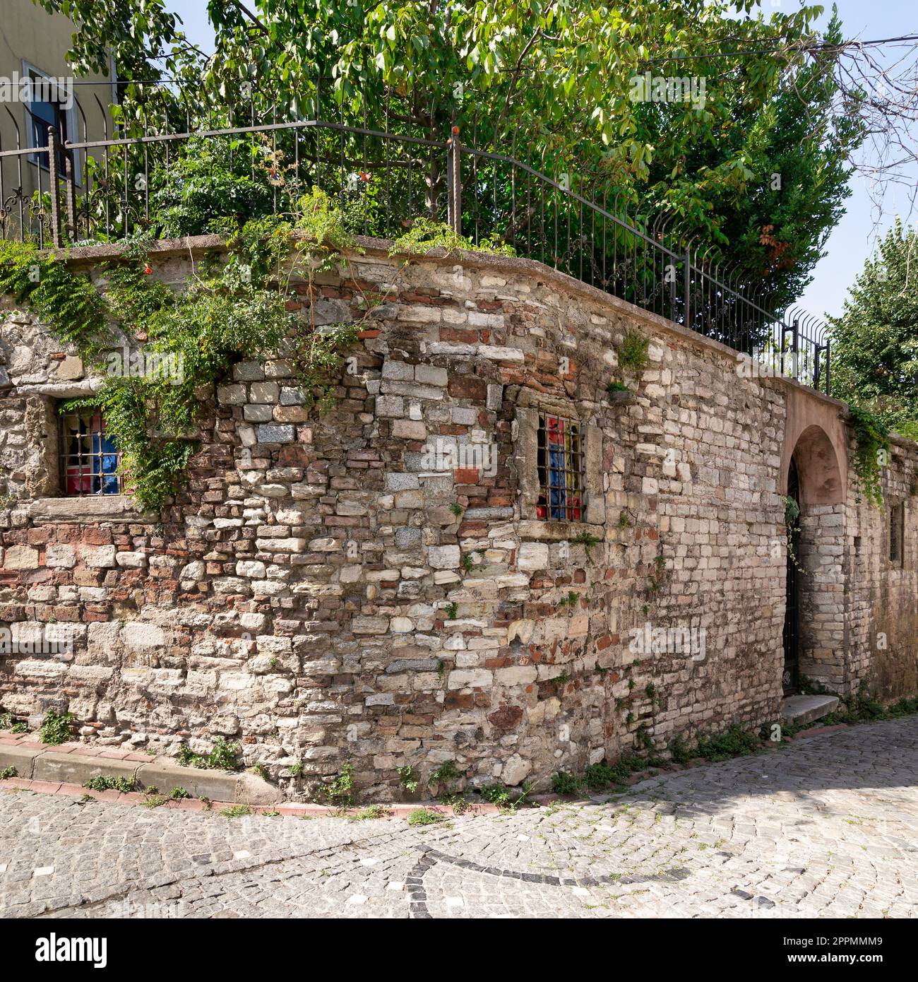 Old abandoned building, with stone wall, wrought iron windows, and climber plants, in ...