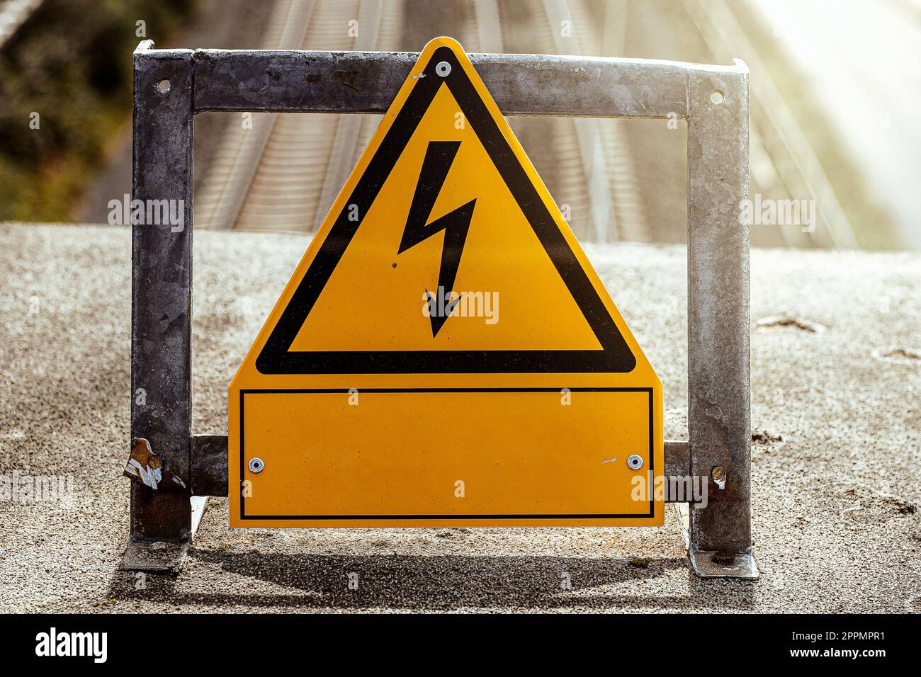 warning sign electricity on a bridge at a railroad track in sunshine ...