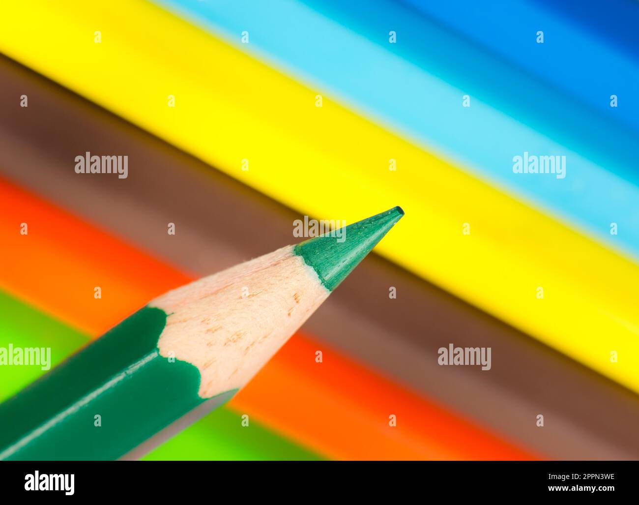 Tip of a green wooden pencil with colored crayons in the background ...