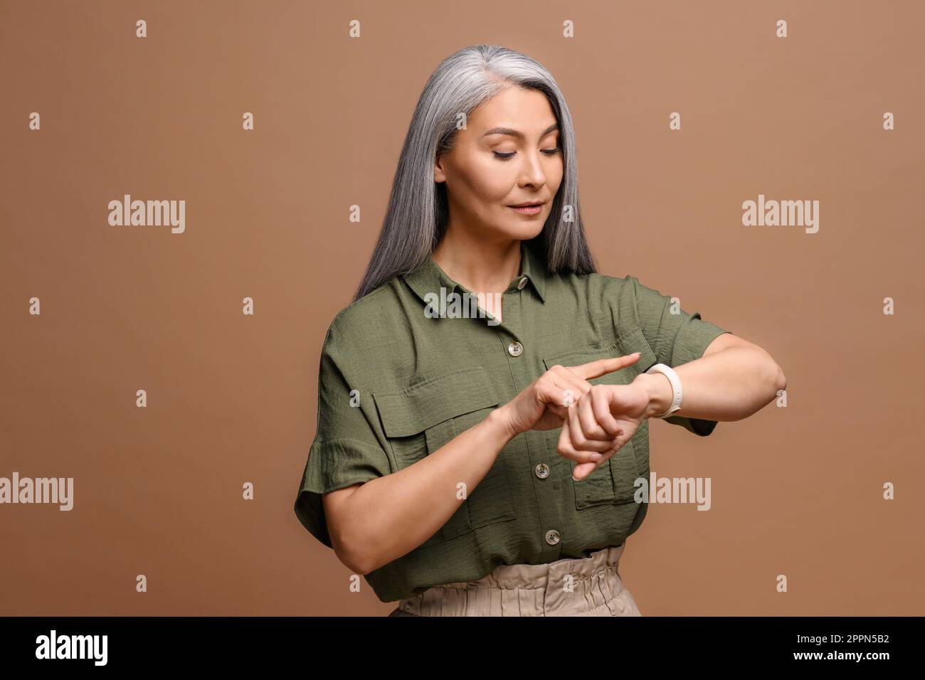 Punctual mature asian woman checking time on wrist watch isolated on ...