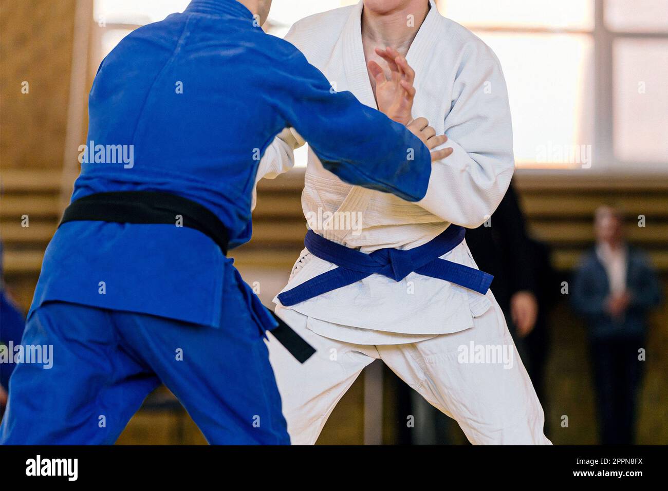 two judoists in blue and white kimono stand compete against each other ...